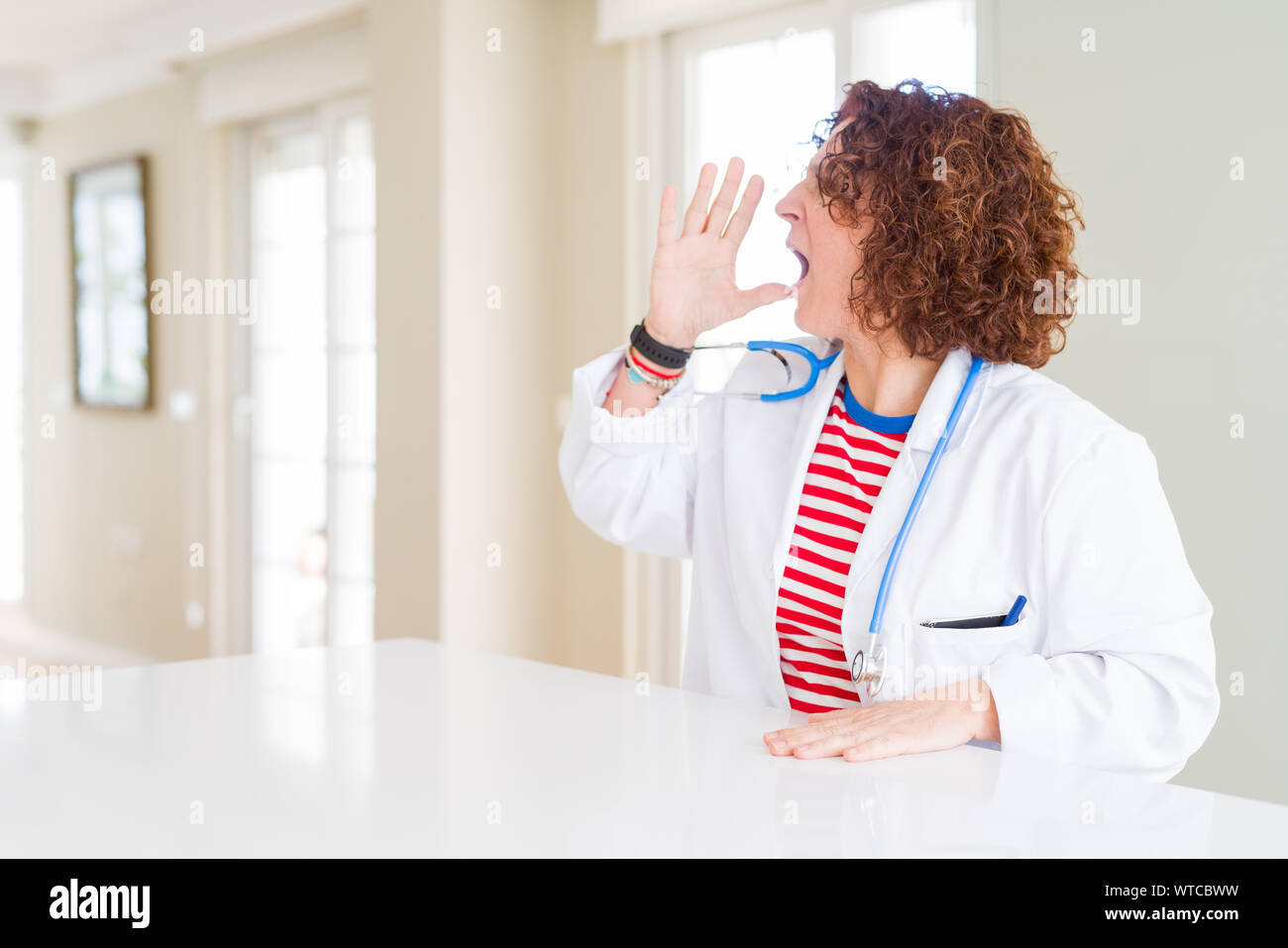 Senior doctor woman wearing medical robe at the clinic shouting and ...