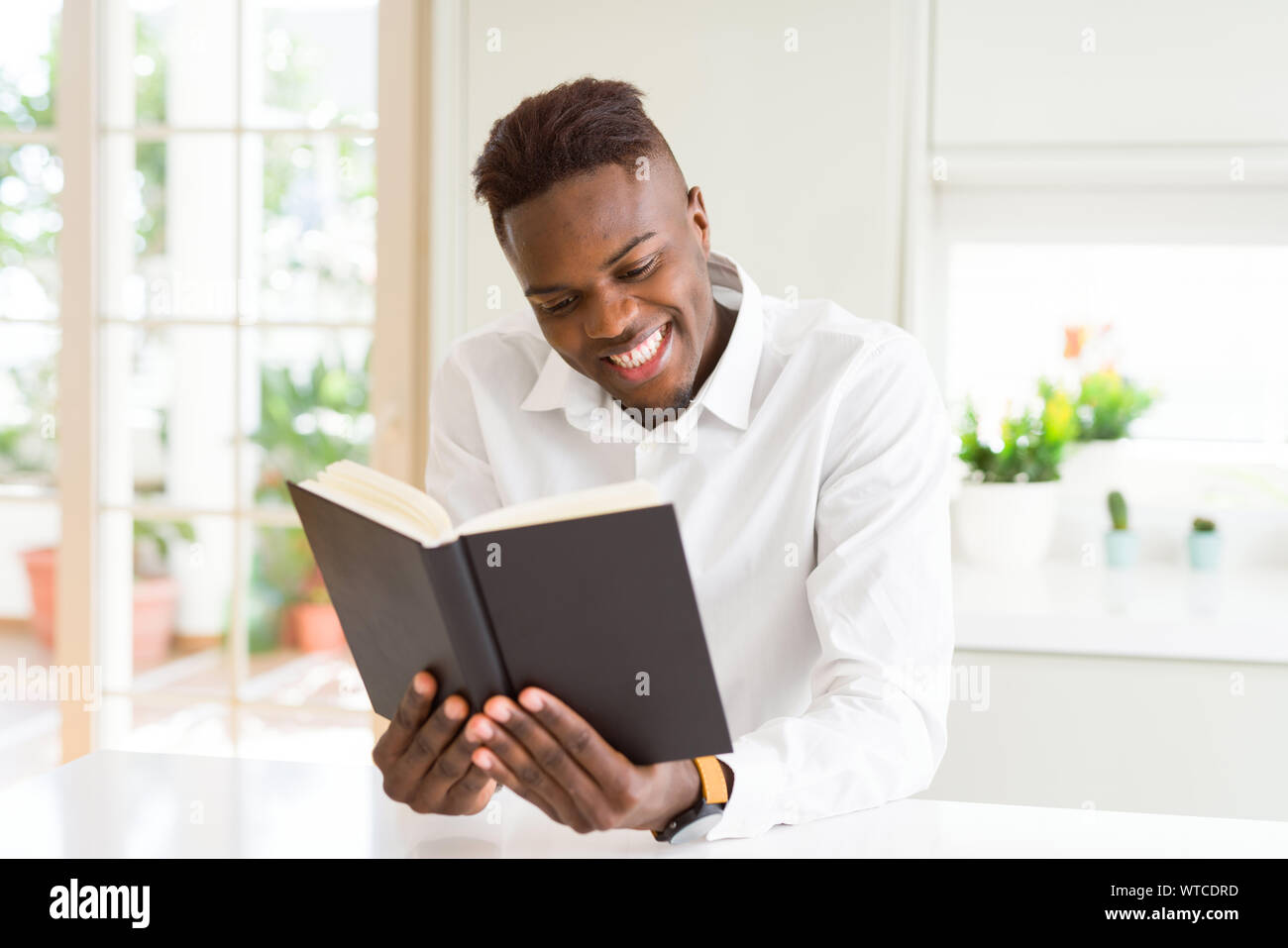 Young african man reading a book, studying for univeristy smiling ...