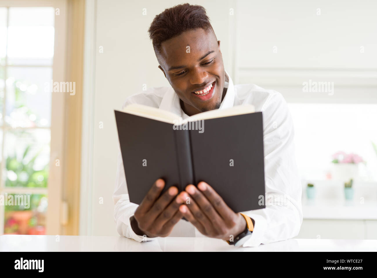 Young african man reading a book, studying for univeristy smiling ...
