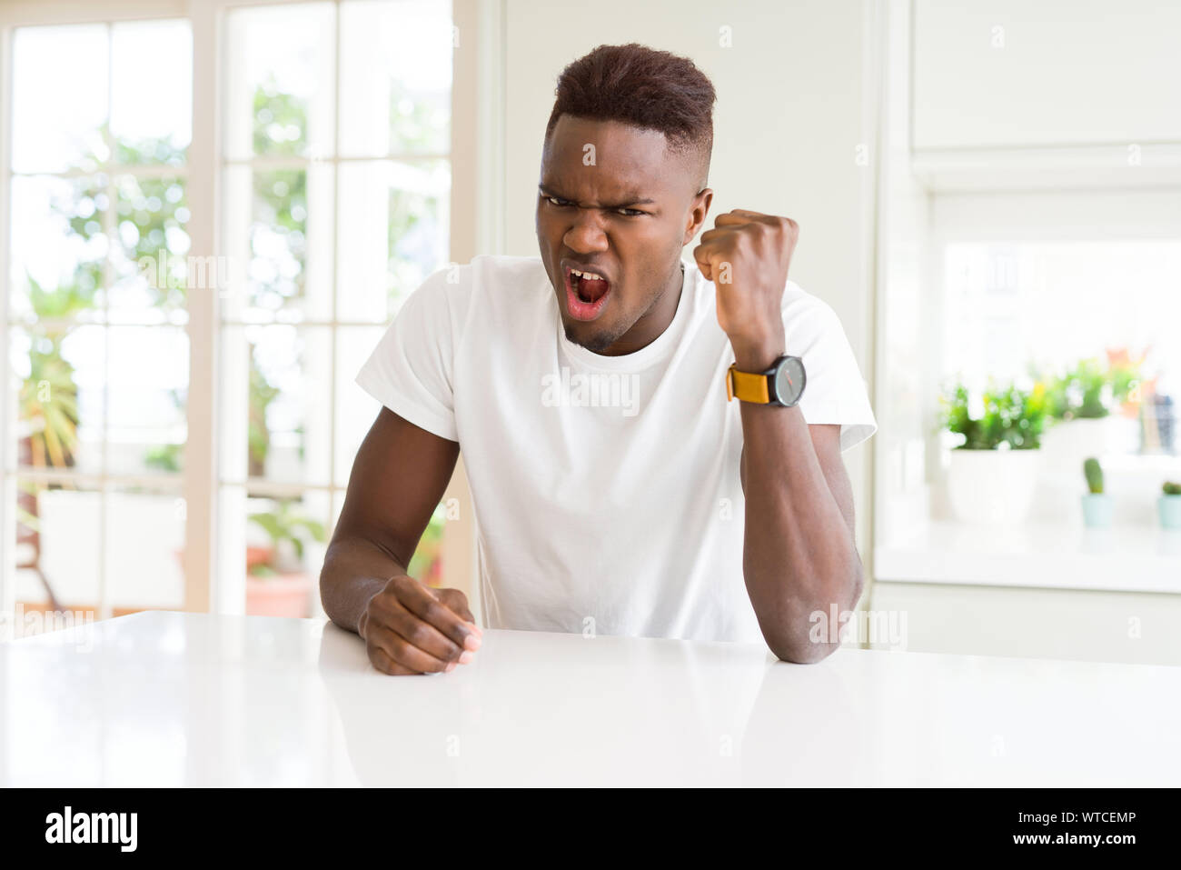 Handsome african american man on white table at home angry and mad ...