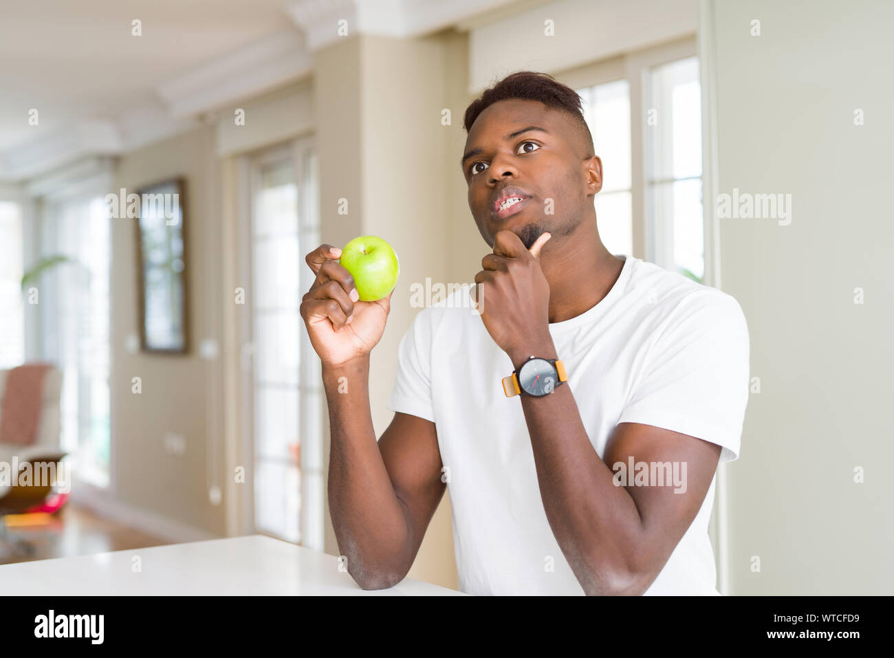 Young african american man eating fresh green apple serious face ...