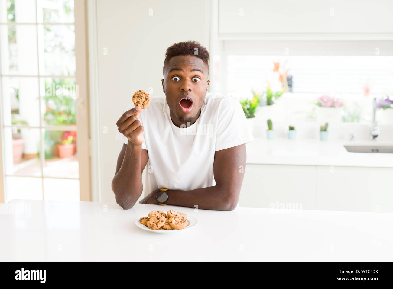Young african american man eating chocolate chips cookies scared in ...
