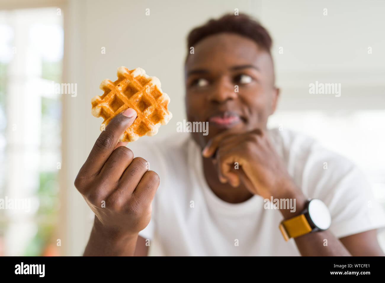 African american man eating sweet Belgian waffle serious face thinking ...