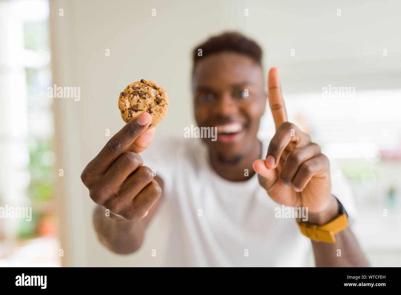Young african american man eating chocolate chips cookies surprised ...