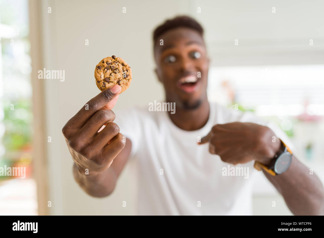 Young african american man eating chocolate chips cookies with surprise ...