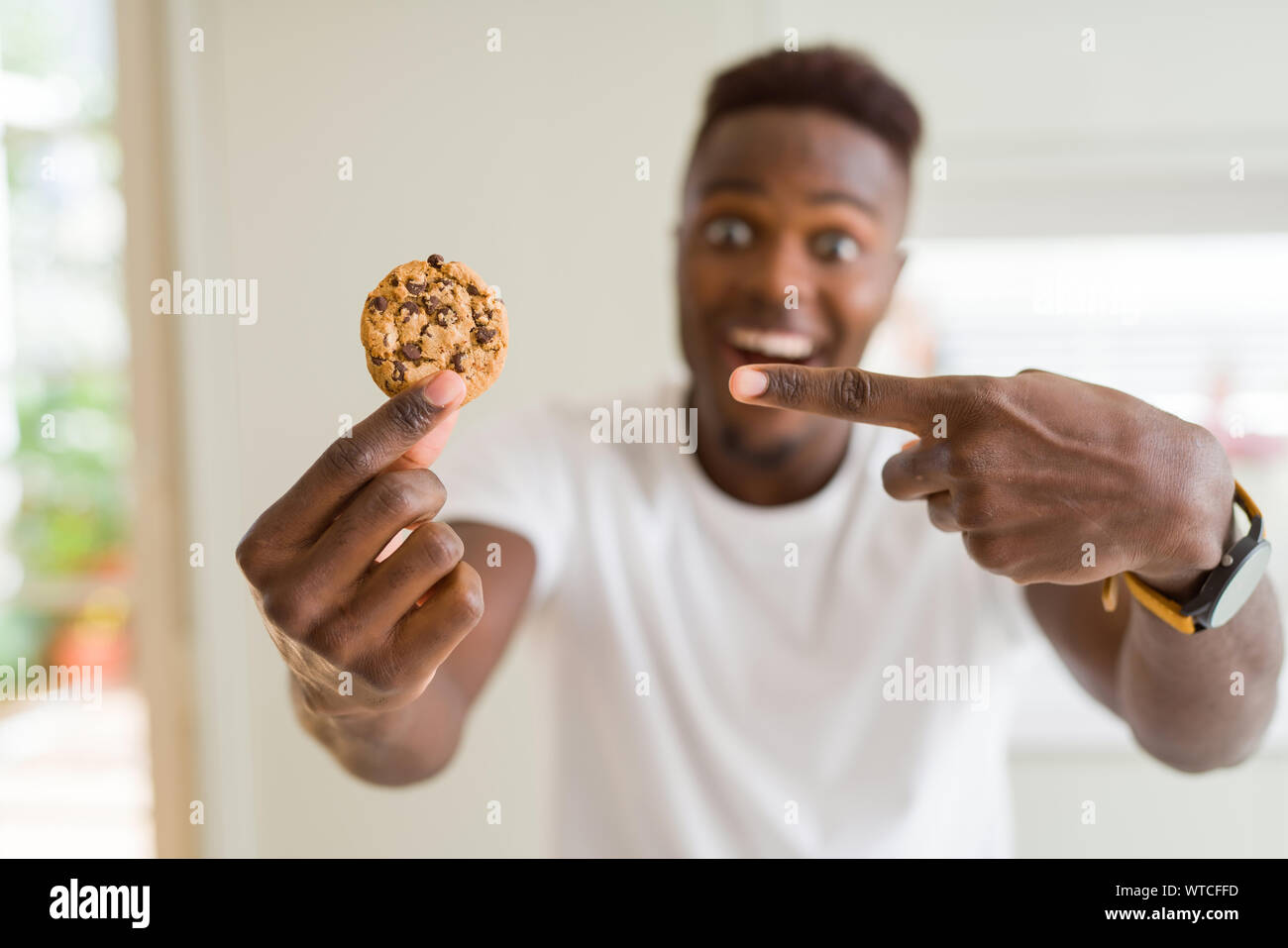 Young african american man eating chocolate chips cookies very happy ...