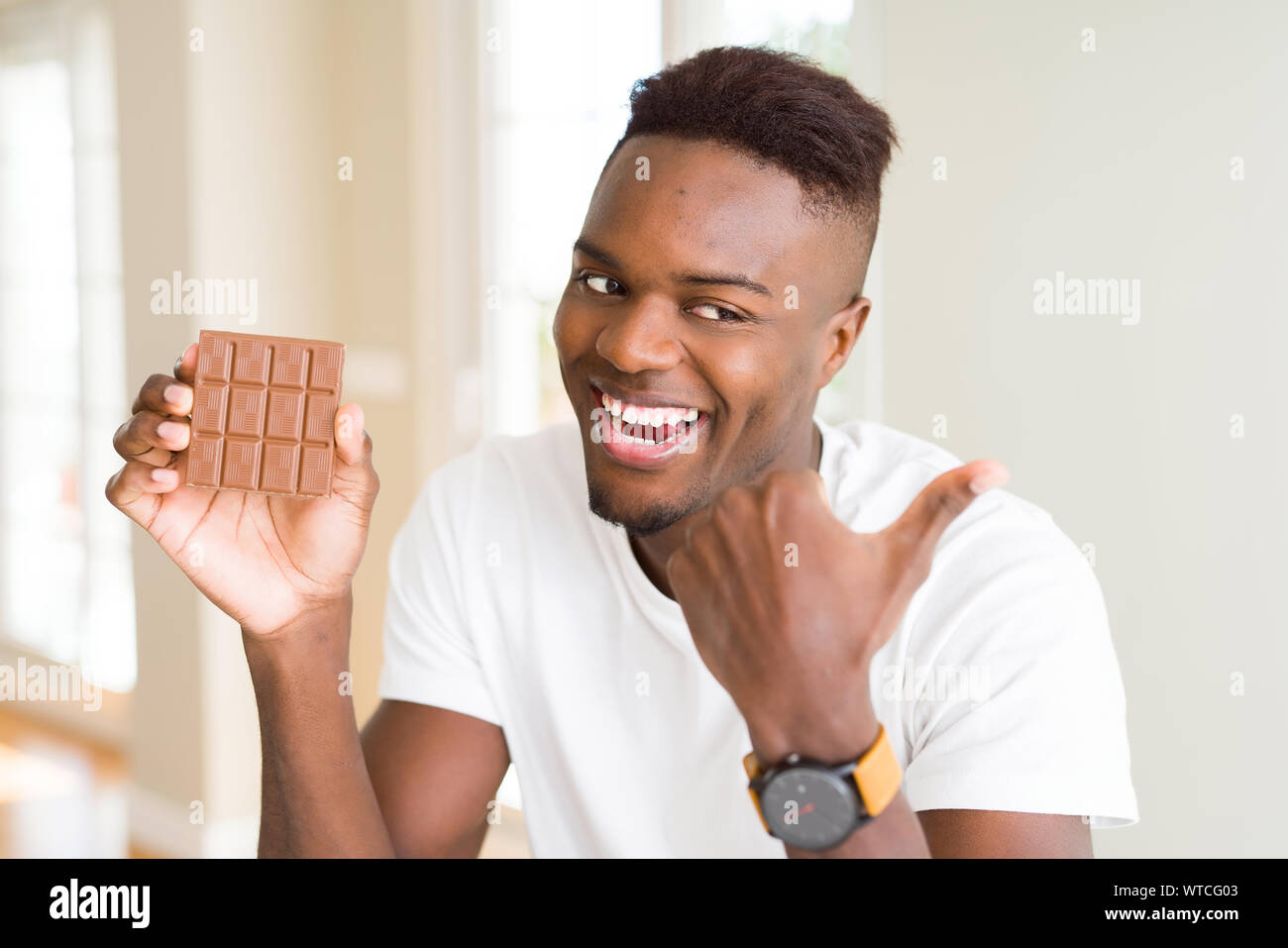 Young african american man eating chocolate bar pointing and showing ...