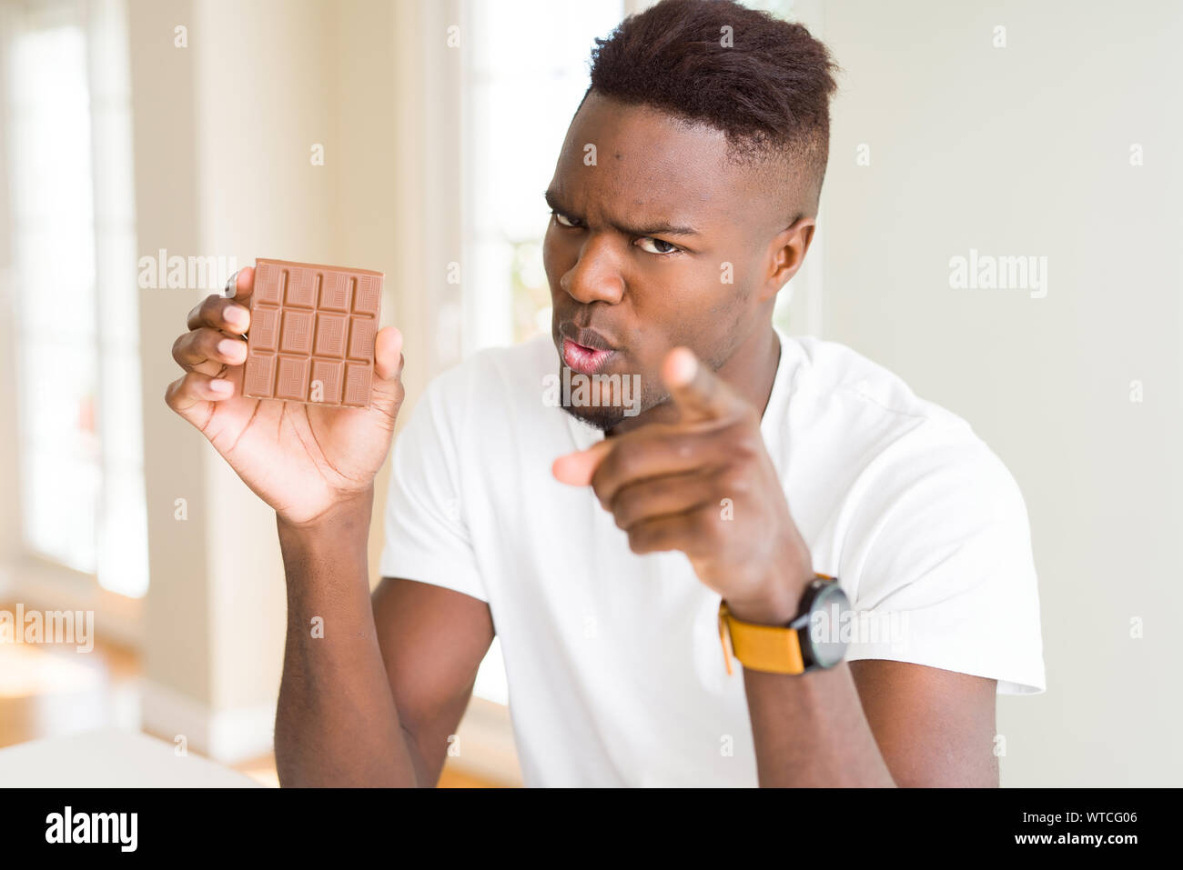 Young african american man eating chocolate bar pointing with finger to ...