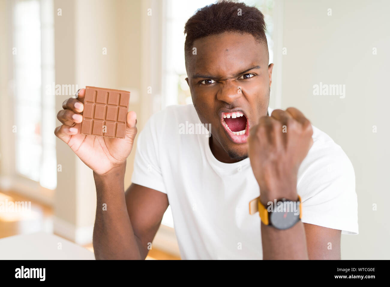 Young african american man eating chocolate bar annoyed and frustrated ...