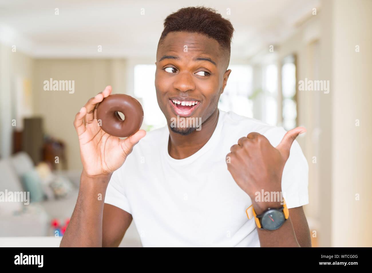African american man eating chocolate donut pointing and showing with ...