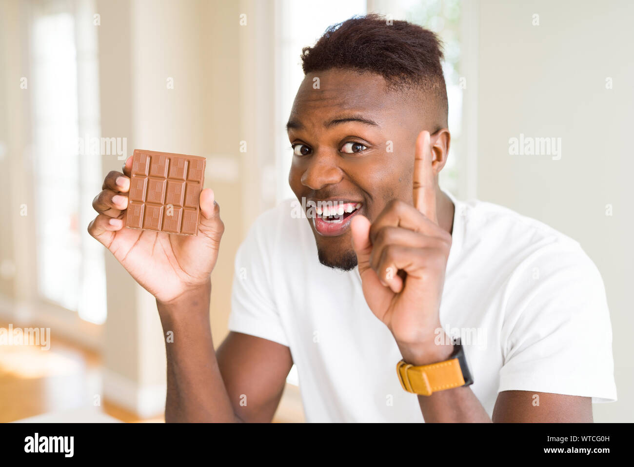Young african american man eating chocolate bar surprised with an idea ...