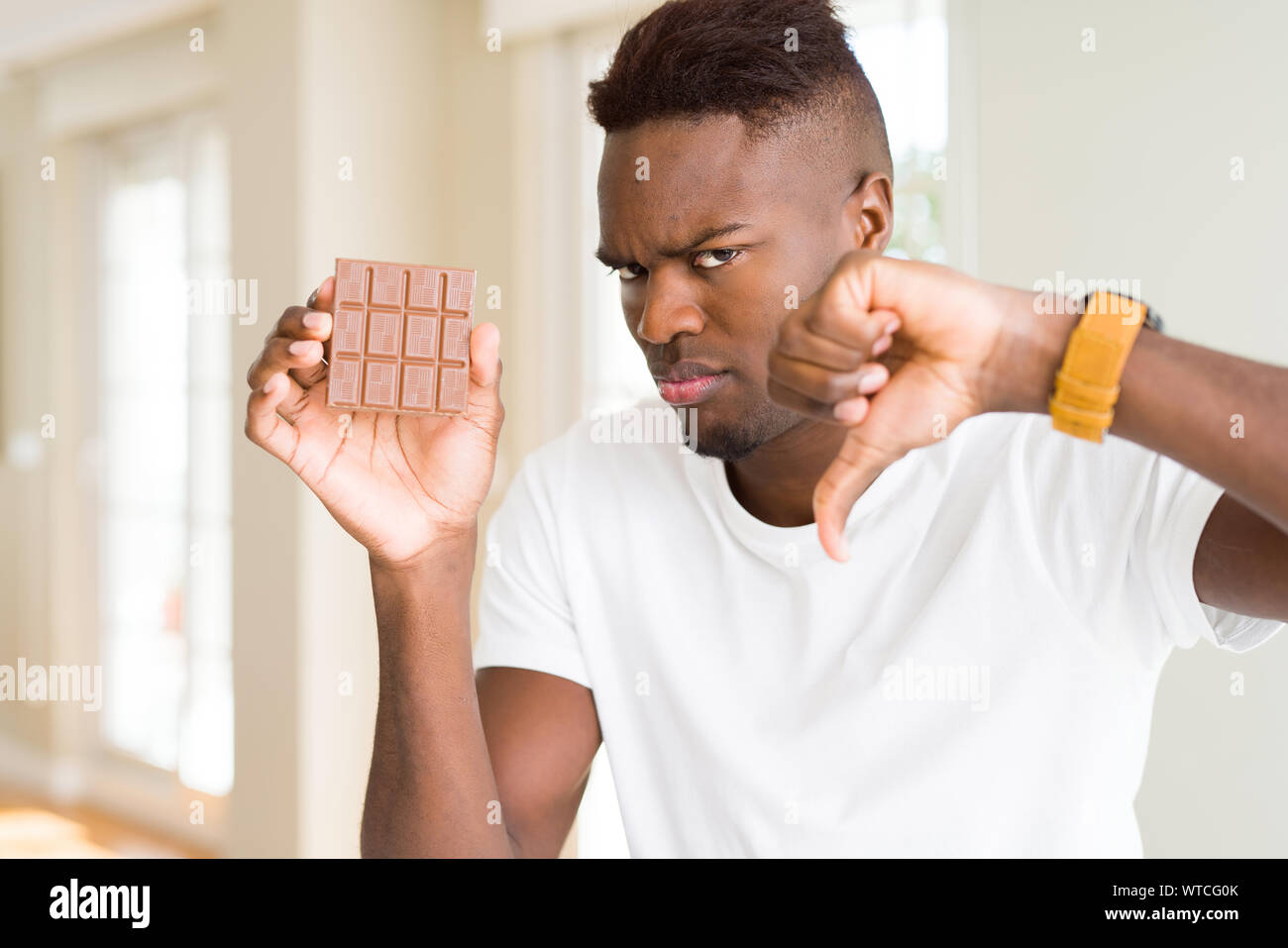 Young african american man eating chocolate bar with angry face ...