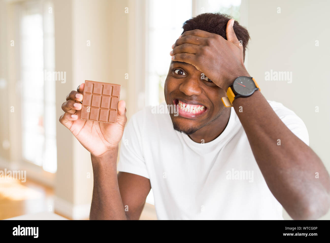 Young african american man eating chocolate bar stressed with hand on ...