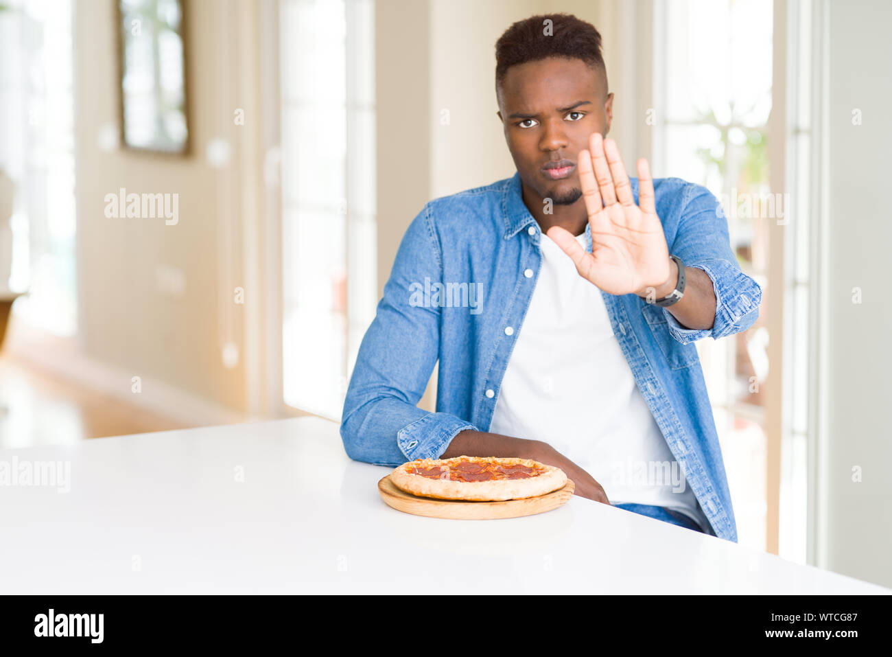 African american man eating pepperoni pizza at home with open hand ...