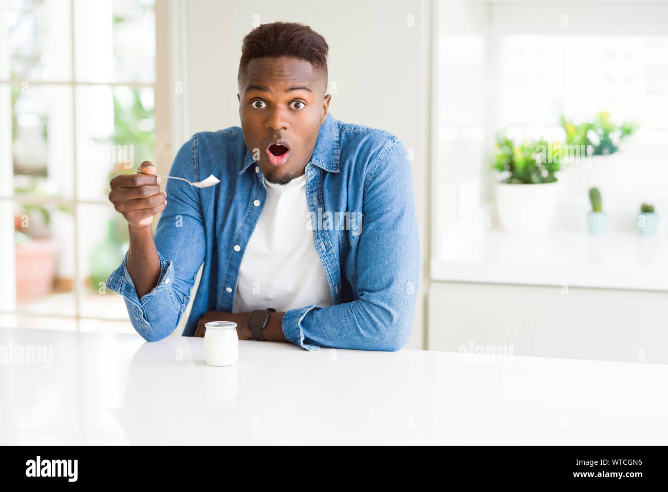 African american man eating healthy natural yogurt with a spoon scared ...