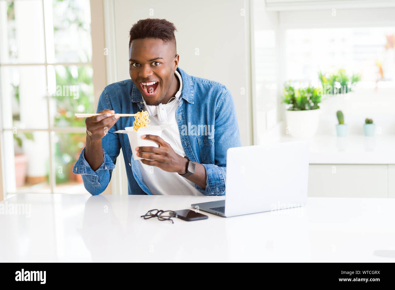 Handsome young african business man eating delivery asian food and ...