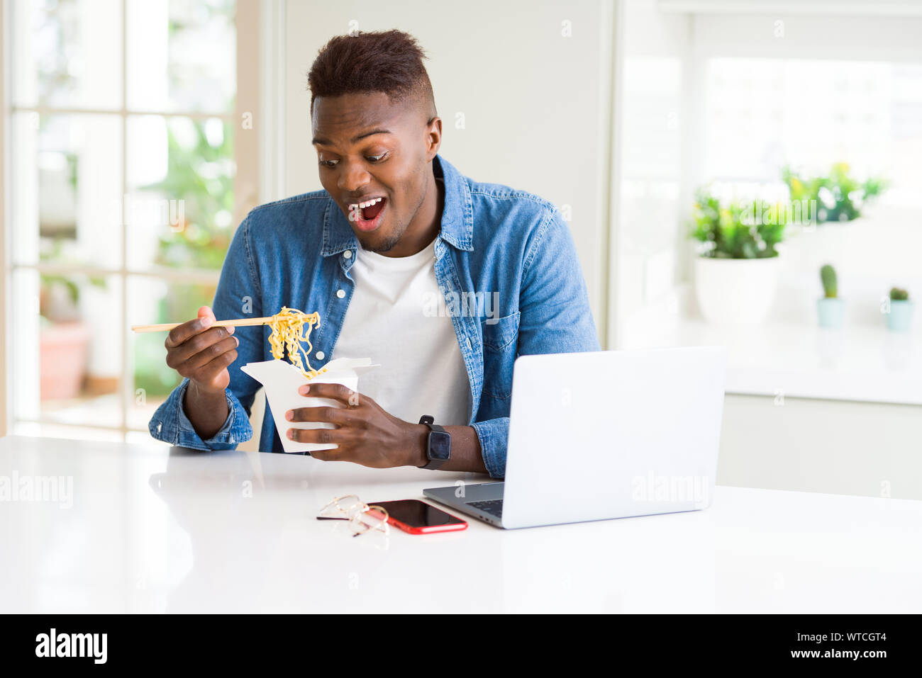 Handsome young african business man eating delivery asian food and ...