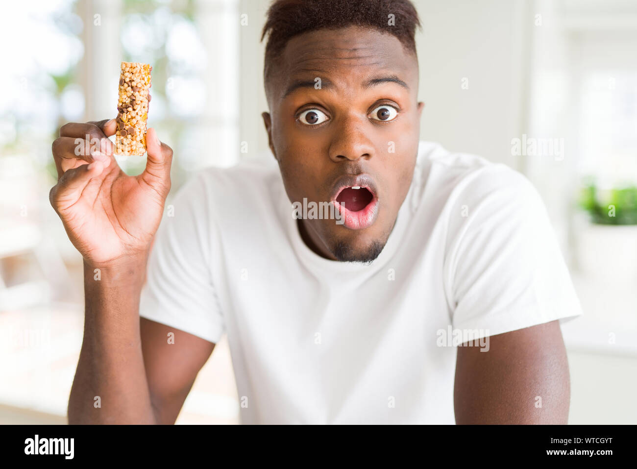 African american man eating energetic cereals bar scared in shock with ...