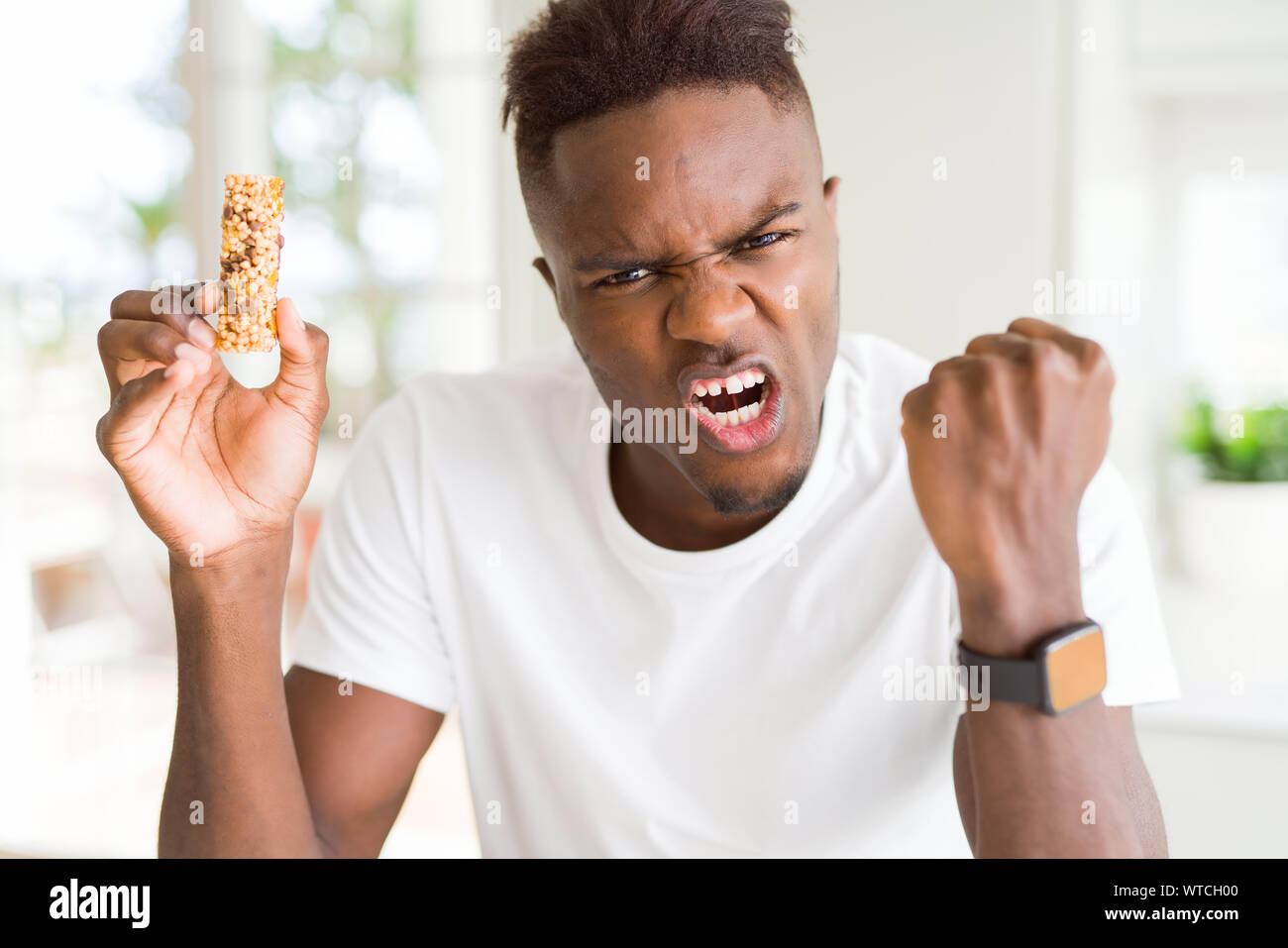 African american man eating energetic cereals bar annoyed and ...