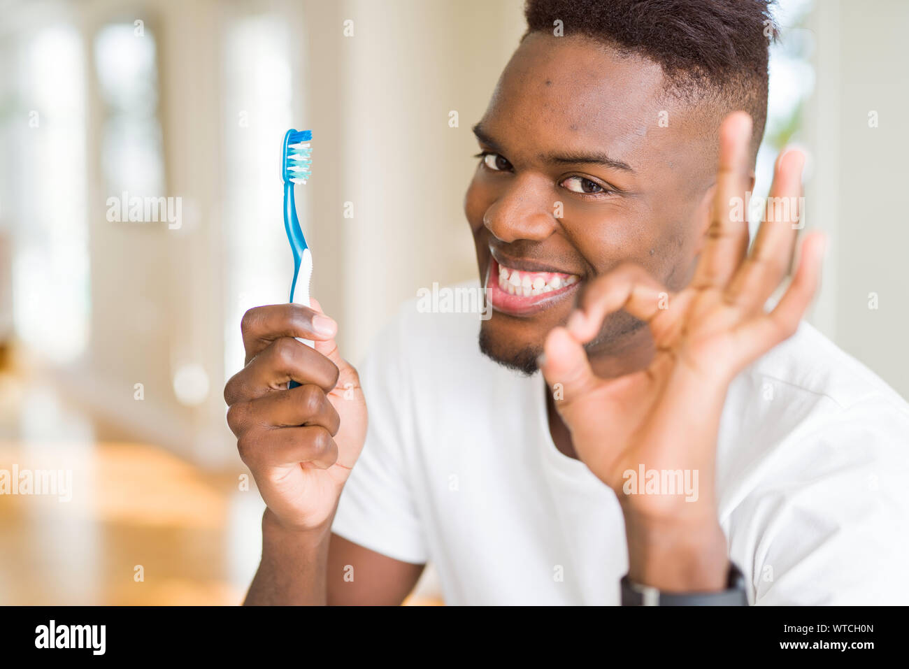 African american man holding toothbrush doing ok sign with fingers ...