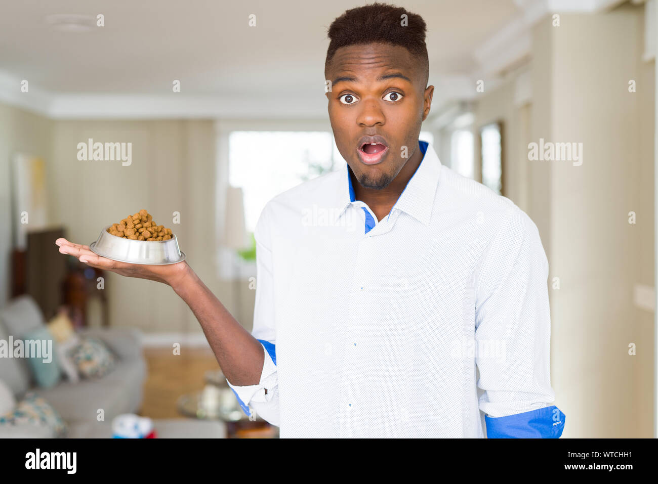 African american man holding metal bowl with cat or dog dry food scared ...