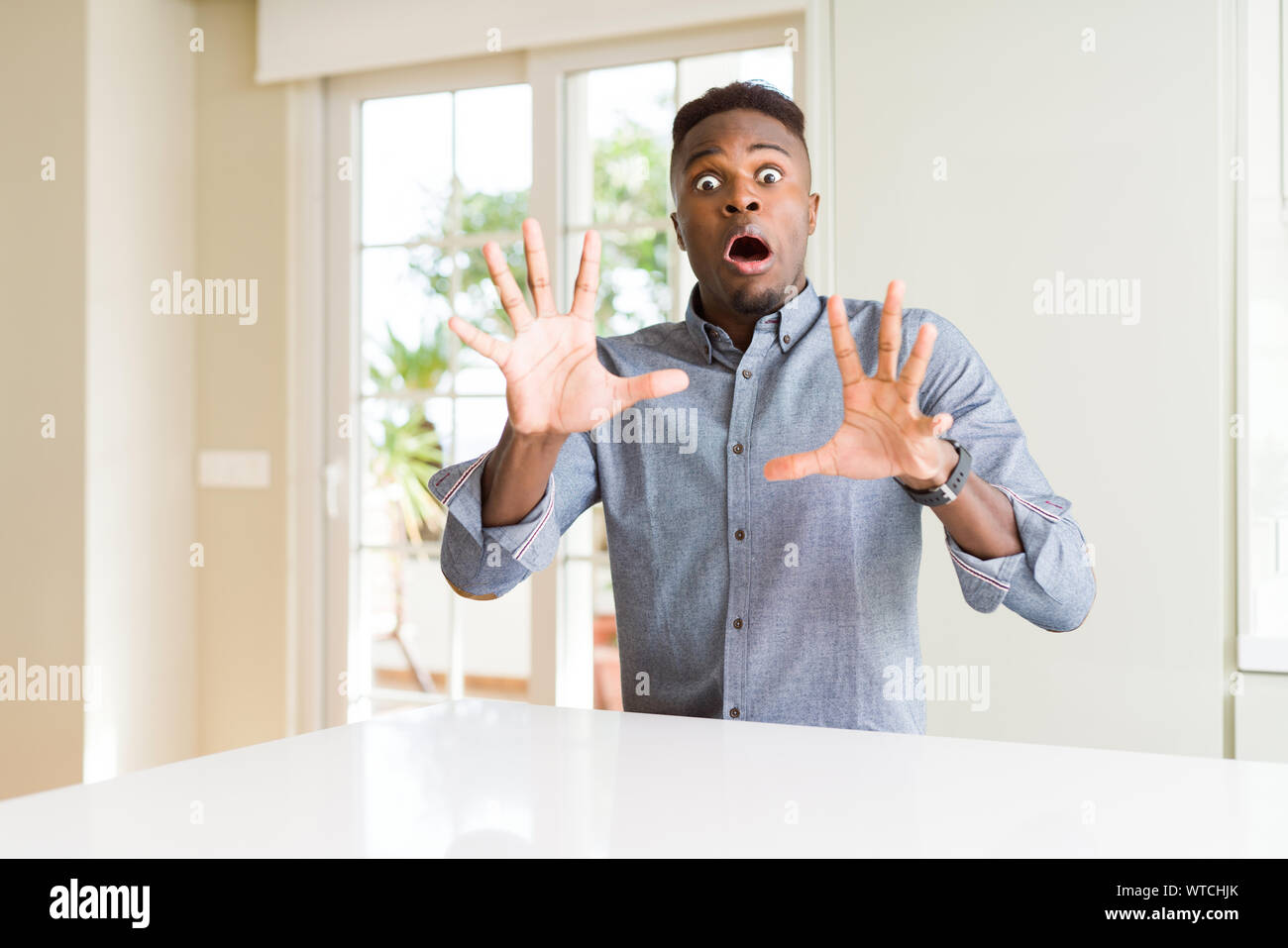 Handsome african american man on white table afraid and terrified with ...