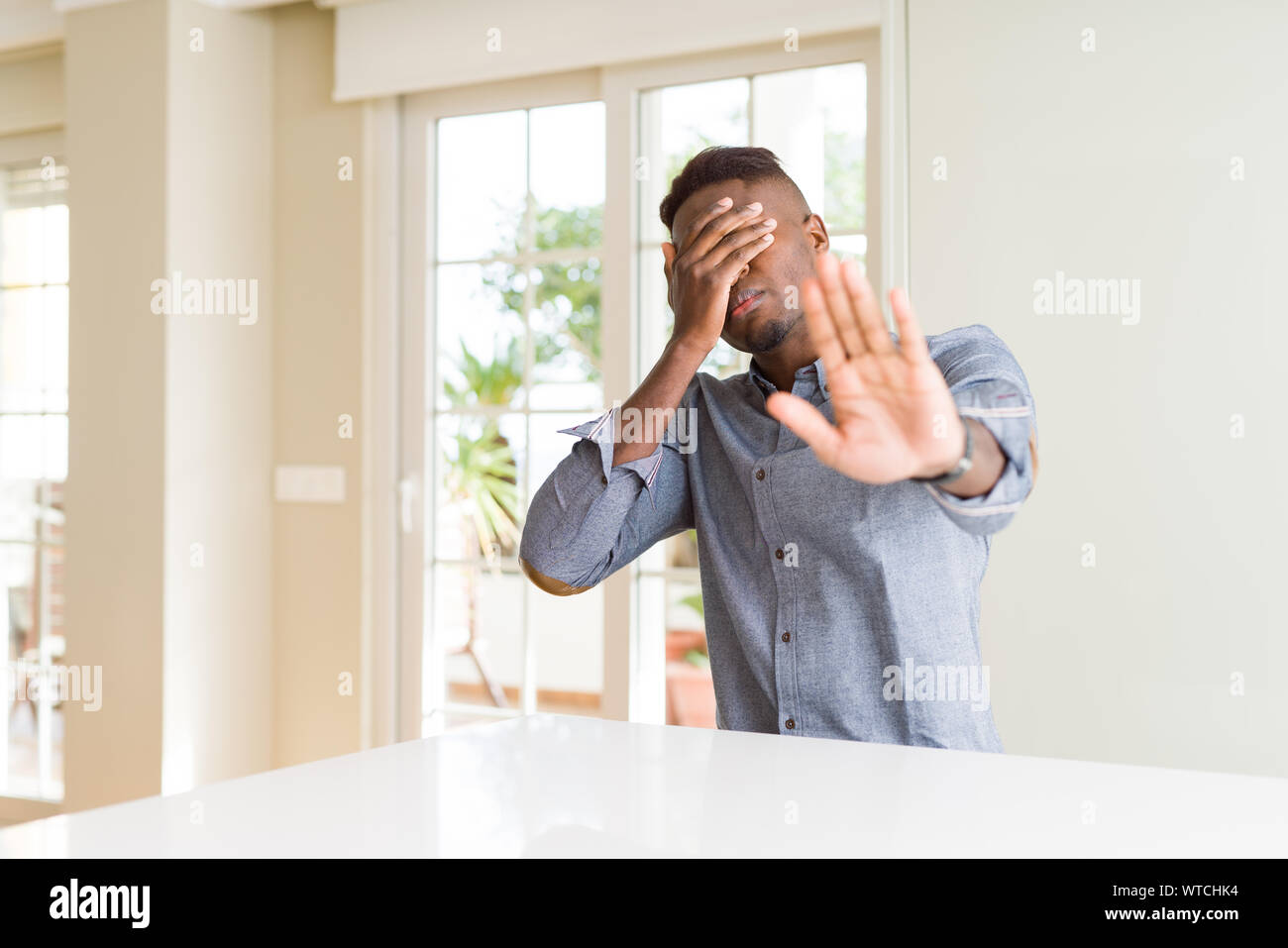 Handsome african american man on white table covering eyes with hands ...