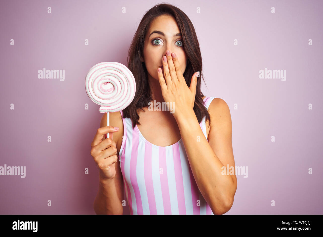 Young beautiful woman eating sweet candy over pink isolated background ...