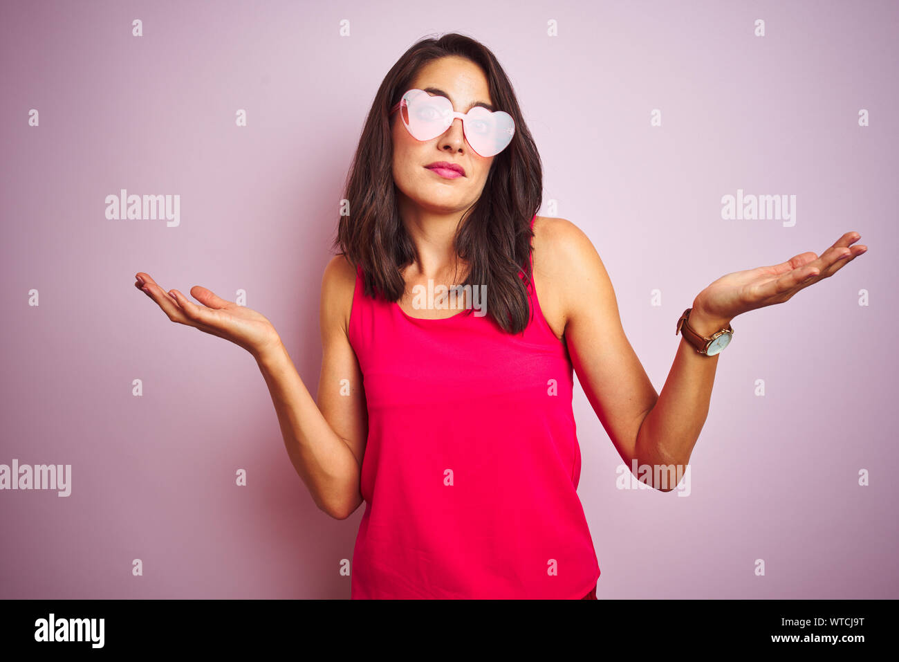 Beautiful woman wearing funny pink heart shaped sunglasses over pink ...