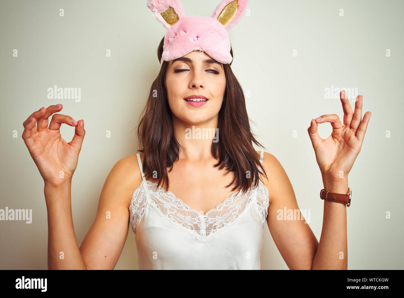 Young beautiful woman wearing pajama and mask standing over white ...