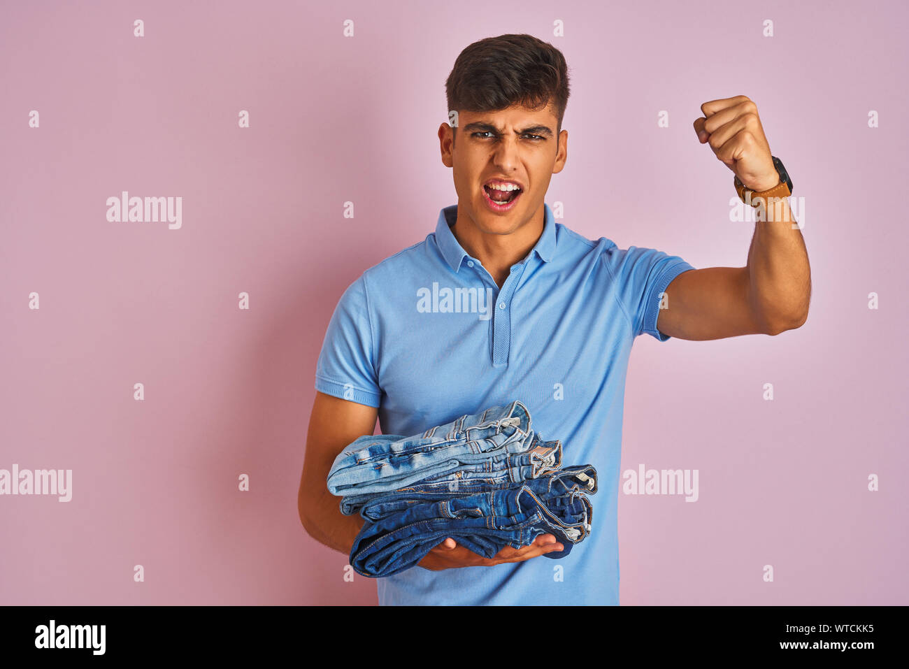 Young indian shopkeeper man holding folded jeans standing over isolated ...