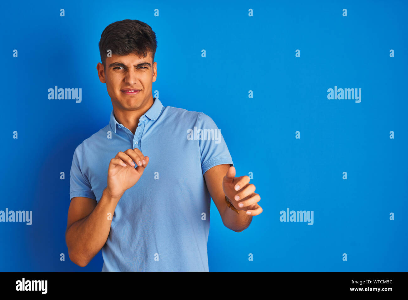 Young indian man wearing casual polo standing over isolated blue ...