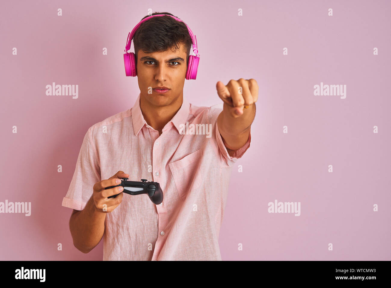 Indian gamer man playing video game using headphones over isolated pink ...