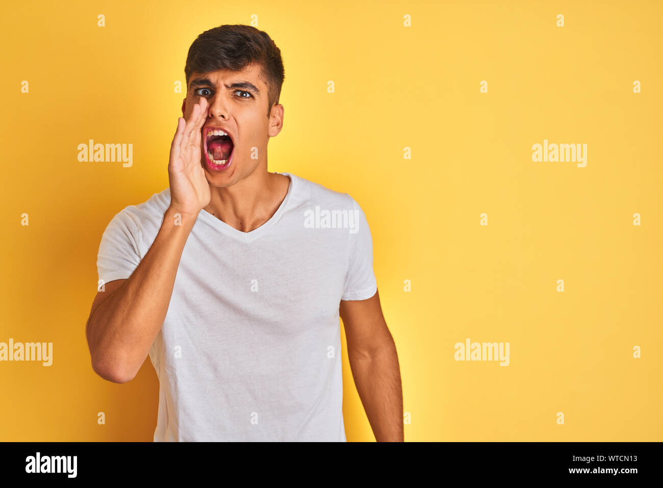 Young indian man wearing white t-shirt standing over isolated yellow ...