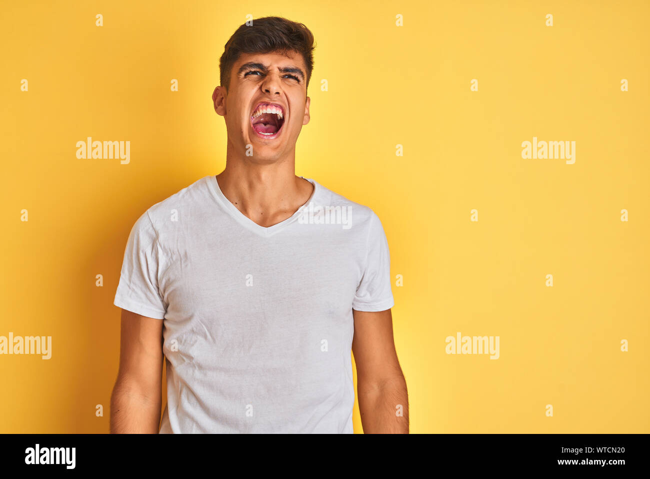 Young indian man wearing white t-shirt standing over isolated yellow ...