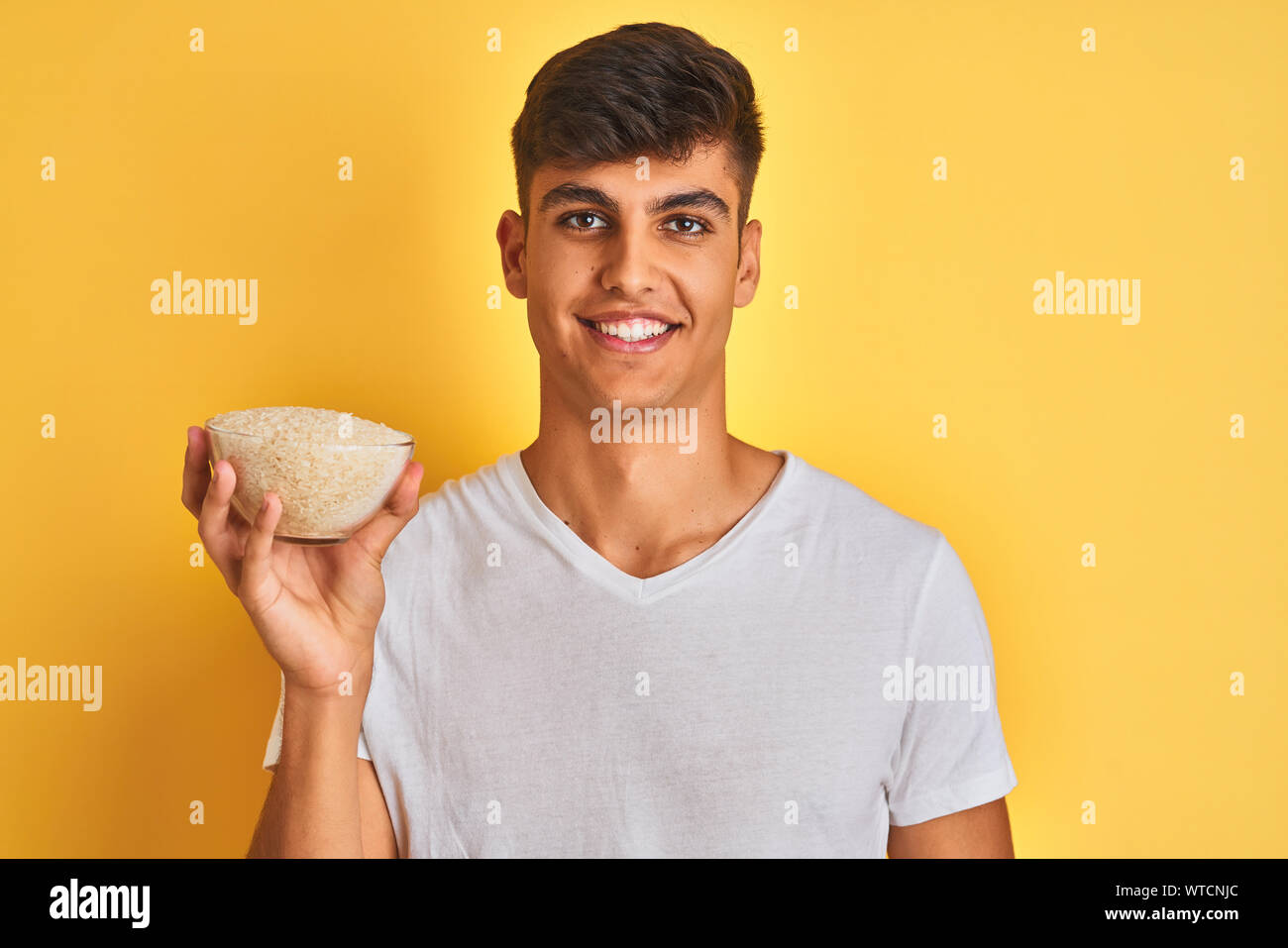 Young indian man holding bowl with rice standing over isolated yellow ...