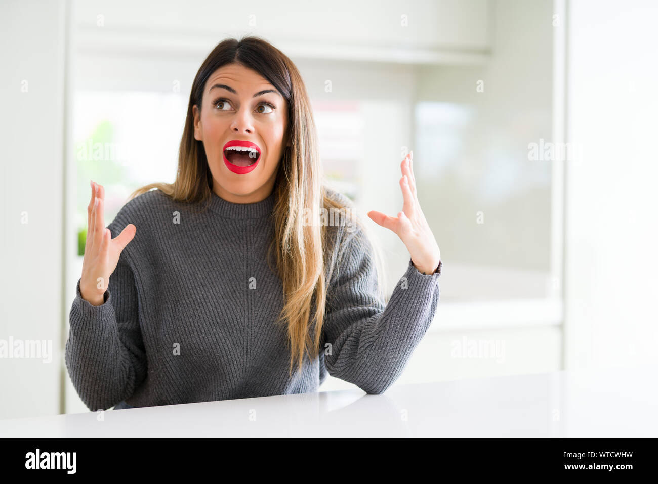 Young beautiful woman wearing winter sweater at home crazy and mad ...