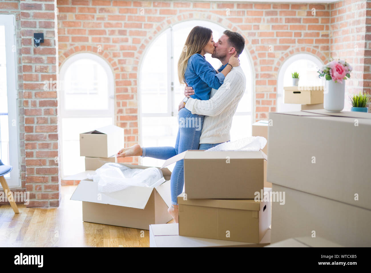 Young beautiful couple hugging and kissing at new home around cardboard ...