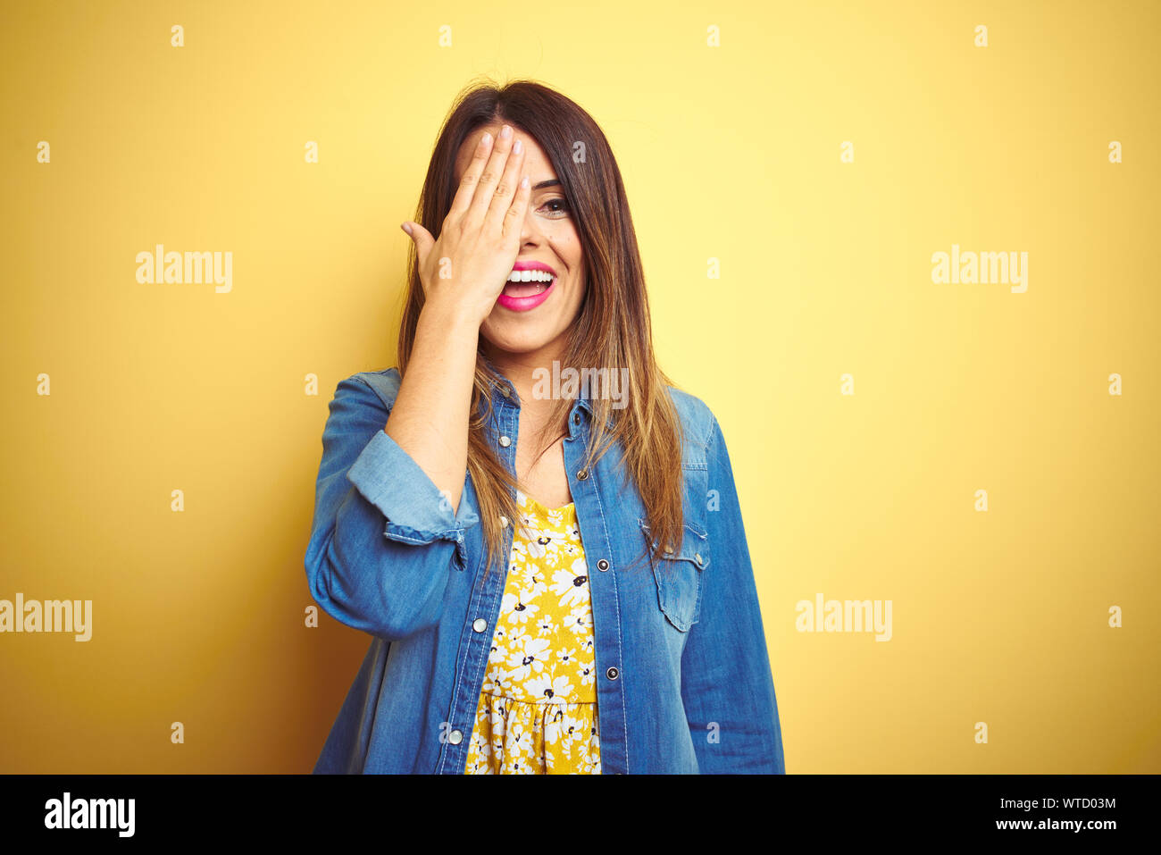 Young beautiful woman standing over yellow isolated background covering ...