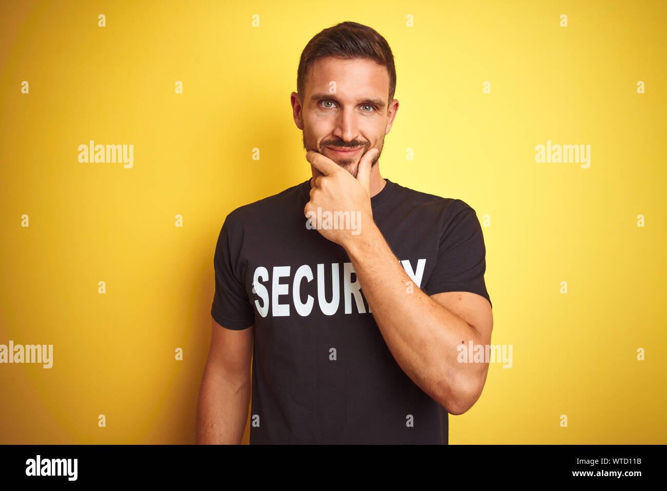 Young safeguard man wearing security uniform over yellow isolated ...