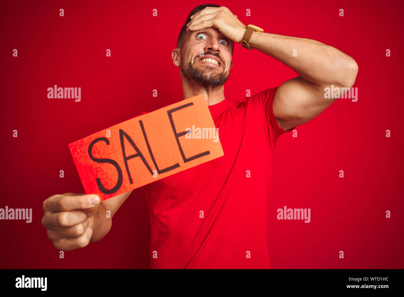 Young man holding sale advertising poster board over red isolated ...