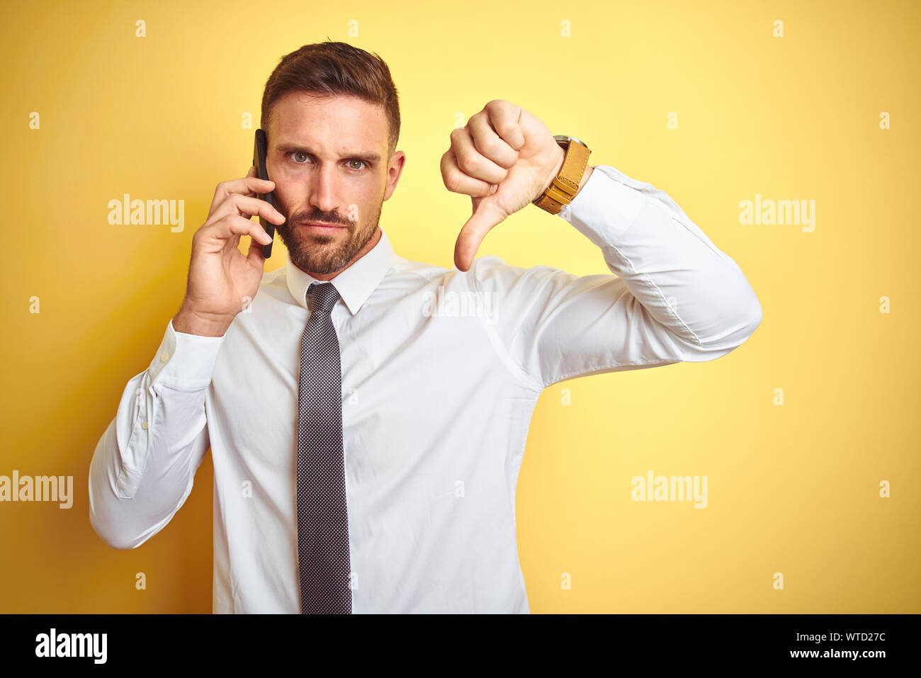 Young handsome business man talking on the phone over yellow isolated ...