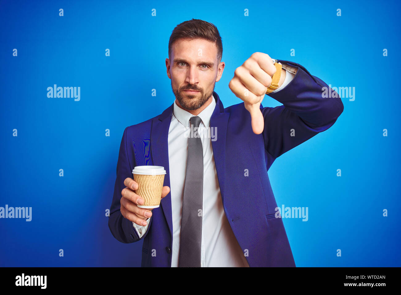 Young handsome business man drinking a coffee on a paper cup over blue ...