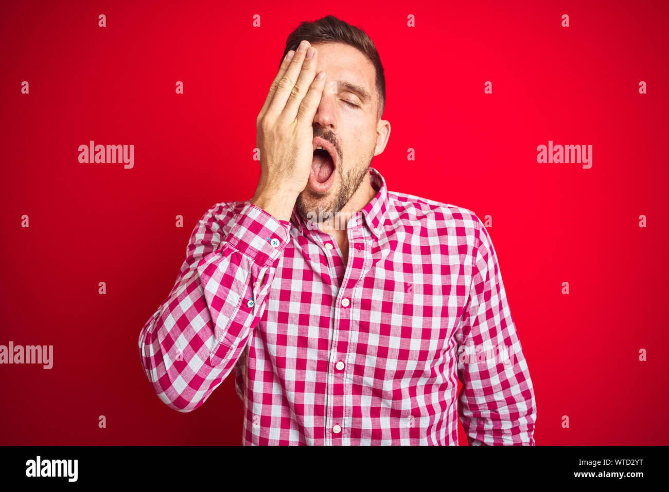 Young handsome man over red isolated background Yawning tired covering ...