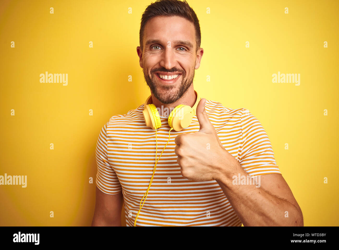 Young handsome man wearing headphones listening to music over yellow isolated background doing ...