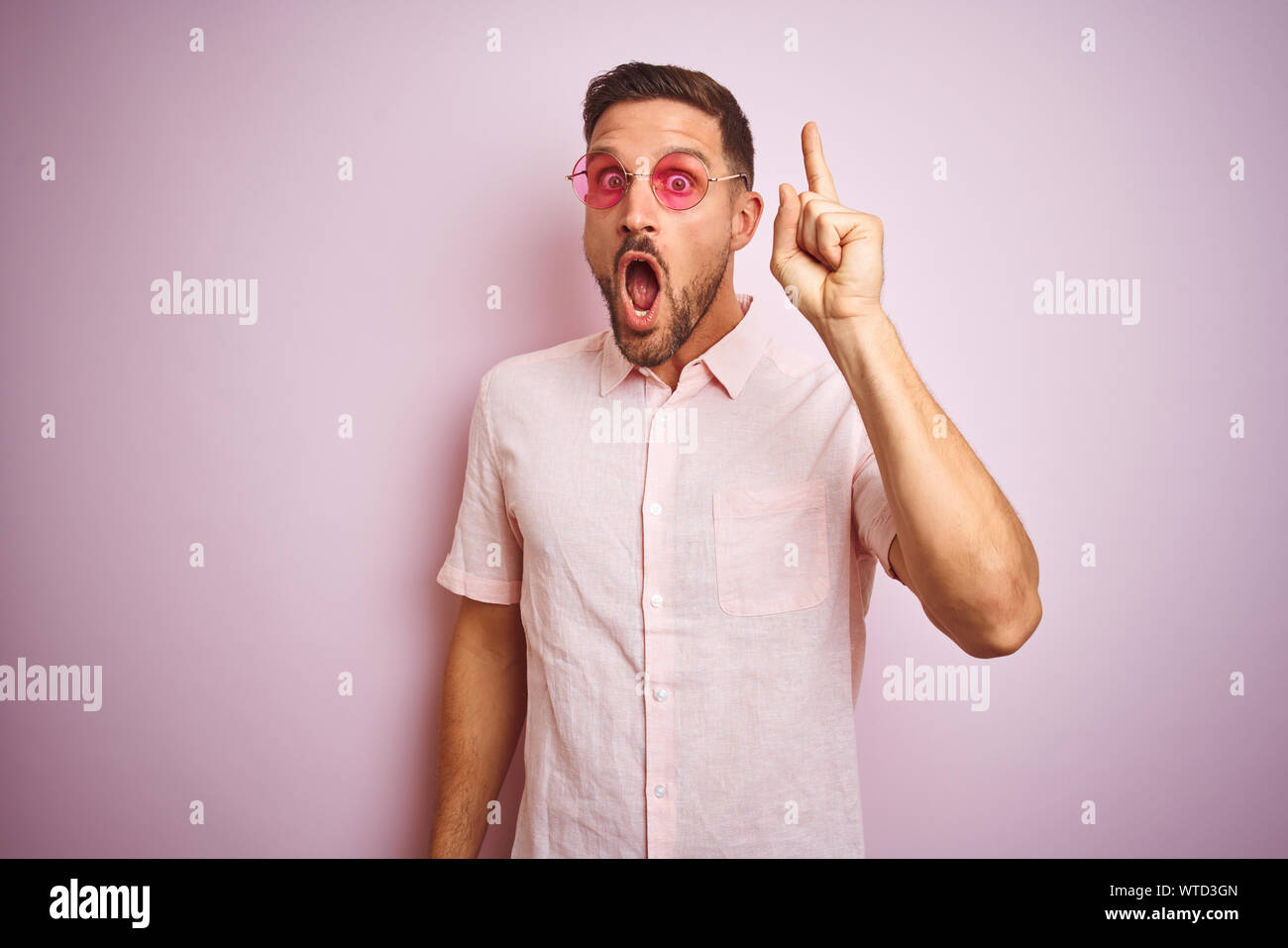 Handsome man wearing elegant summer shirt and sunglasses over pink ...
