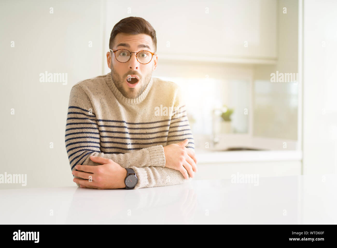 Young handsome man wearing glasses at home scared in shock with a ...