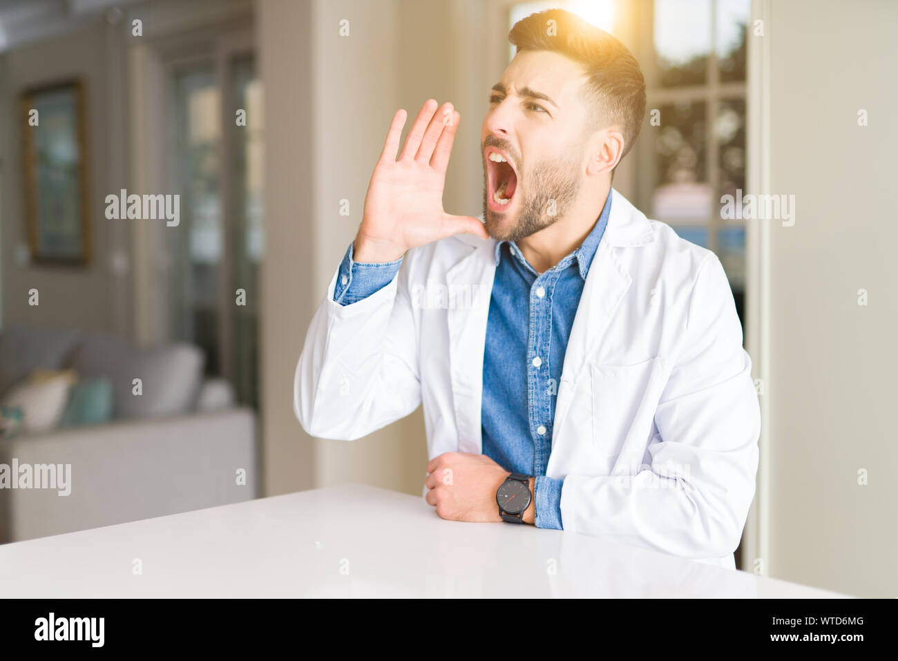 Young handsome doctor man at the clinic shouting and screaming loud to ...