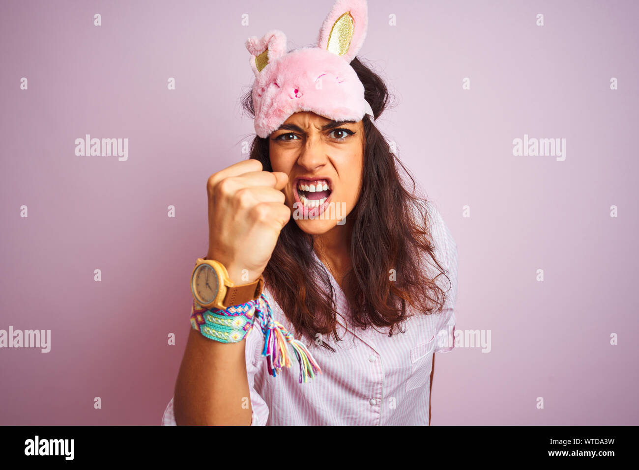 Young beautiful woman wearing pajama and sleep mask over isolated pink ...