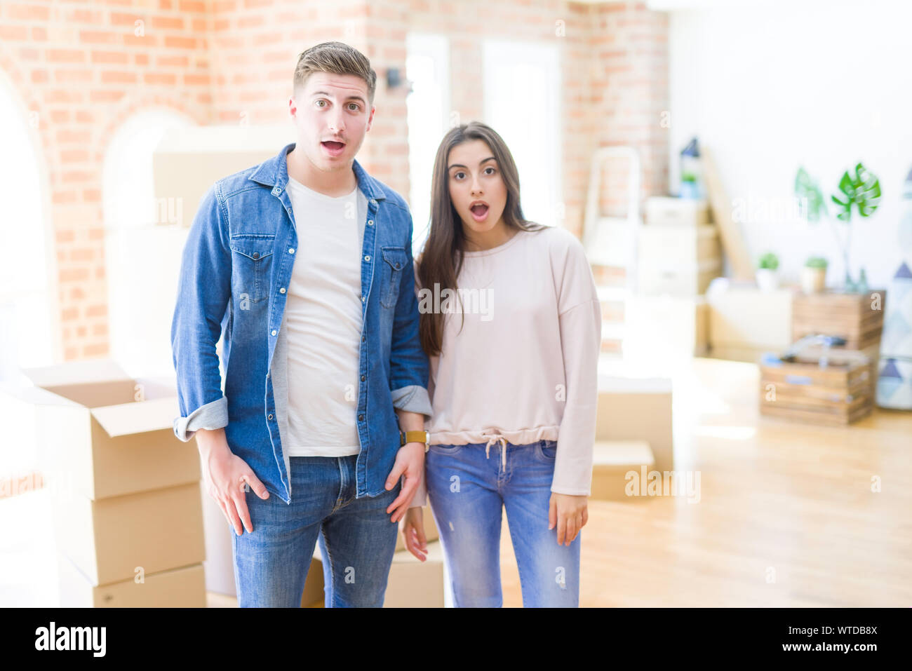 Beautiful young couple moving to a new house afraid and shocked with ...